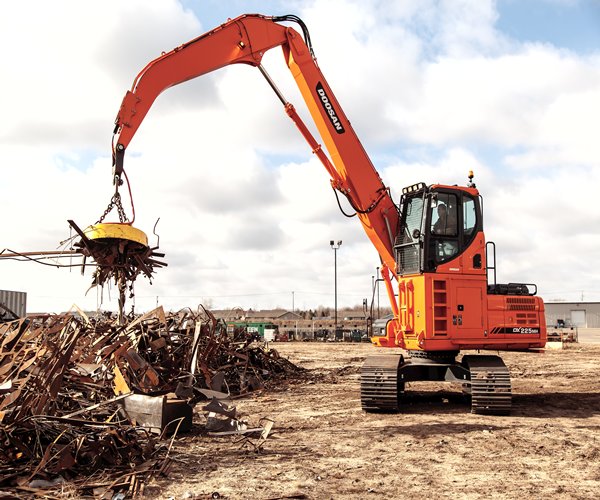 Doosan DX225MH-3 lifts scrap metal into a pile with the magnet attachment.